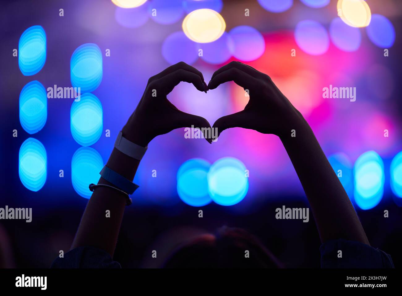 Hands form heart shape at music fest, silhouetted against vibrant stage ...