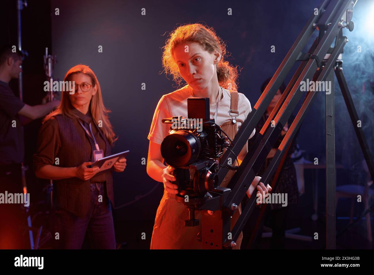 Waist up portrait of camerawoman operating equipment on rig in studio ...
