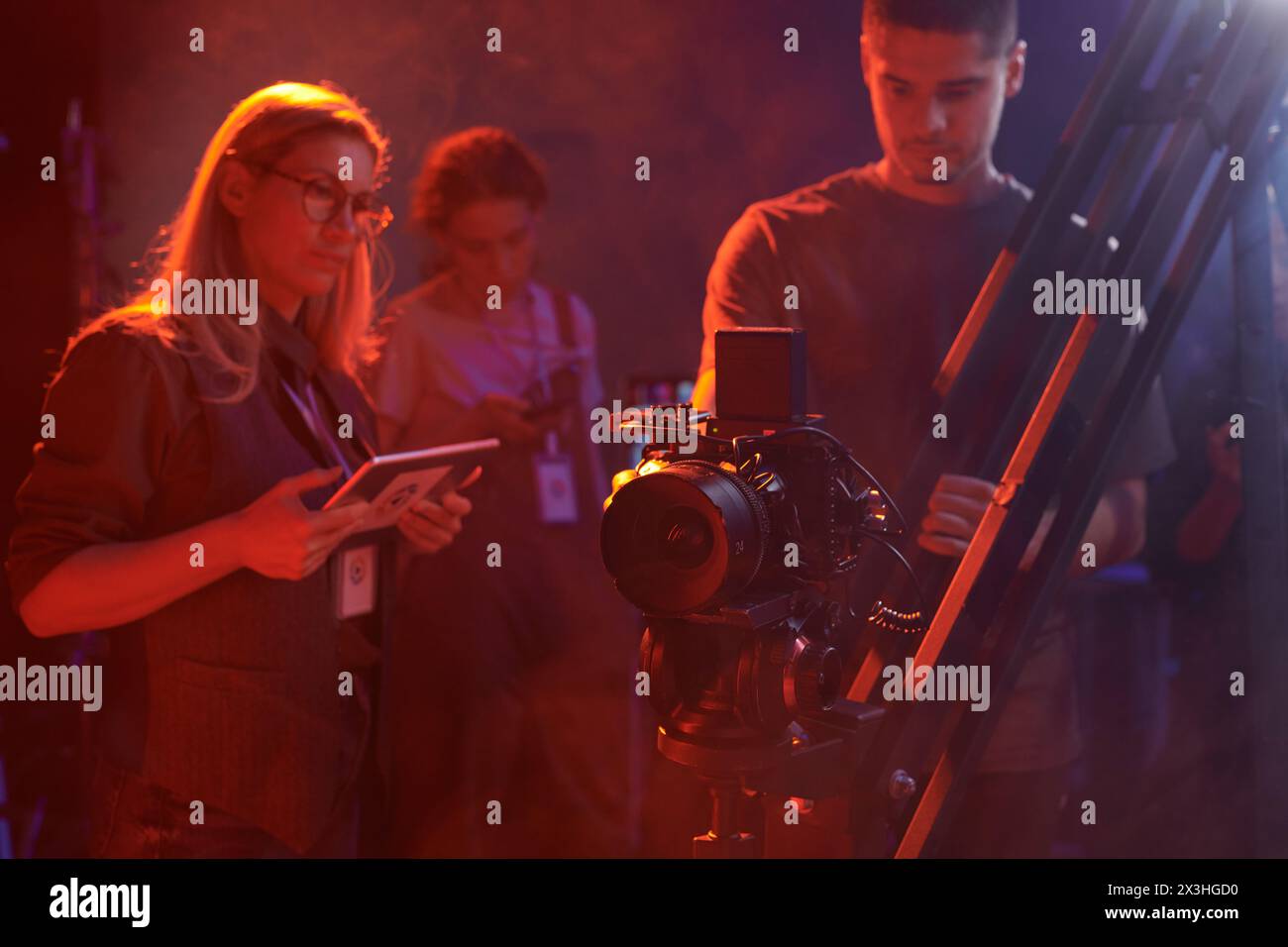 Video production crew working together backstage on set in red neon ...