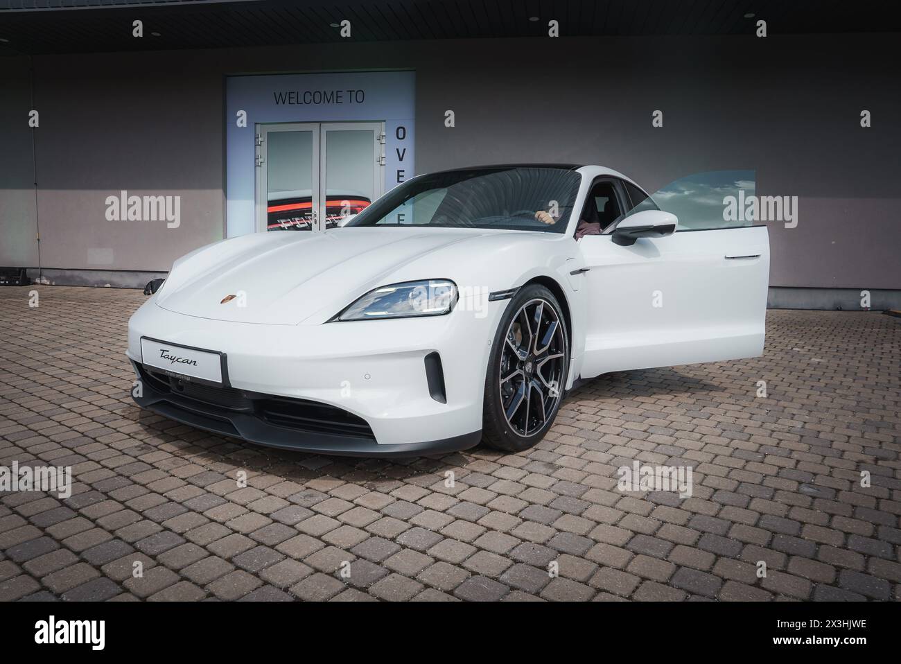 White Porsche Taycan Parked In Front Of Building With WELCOME TO OVER ...