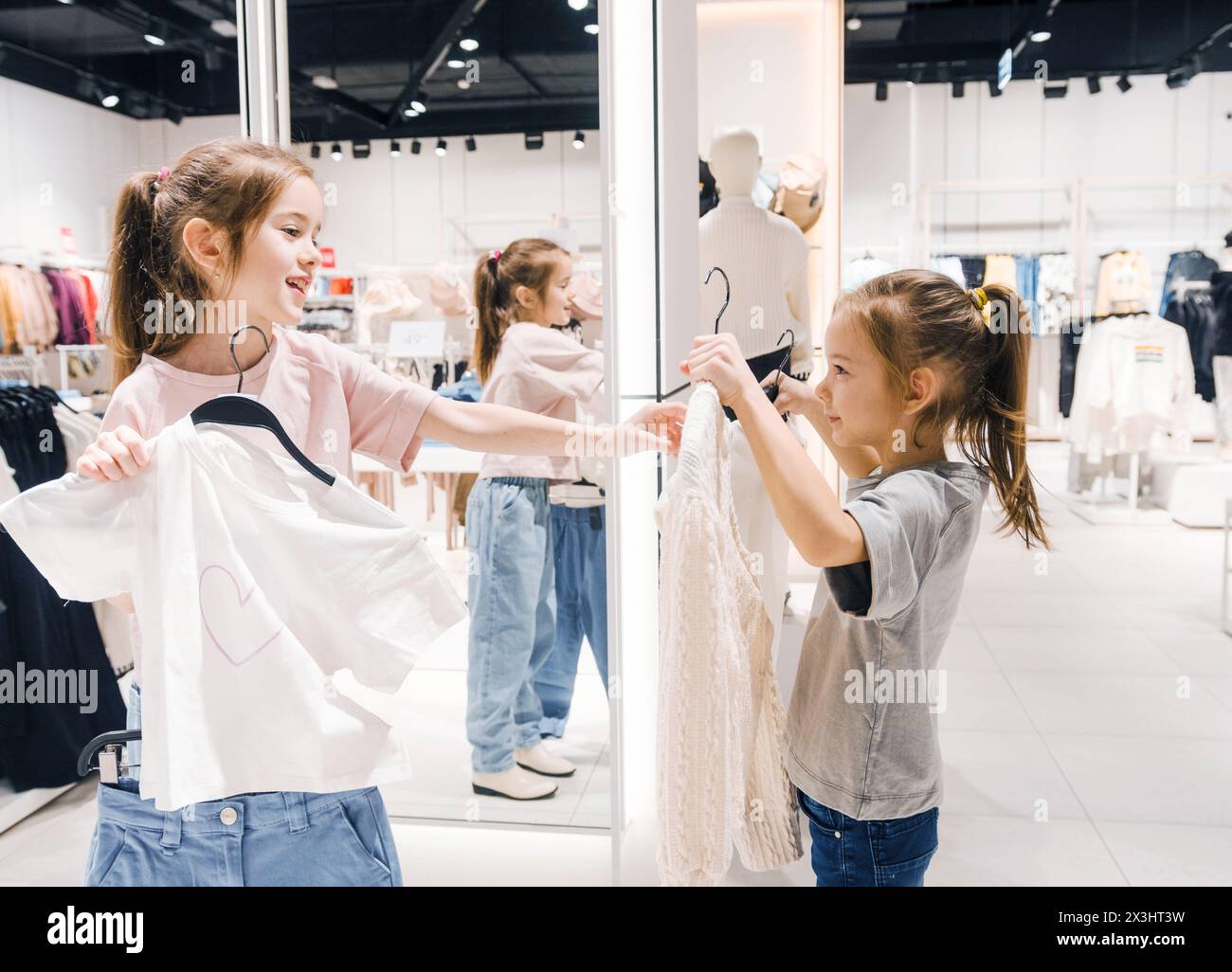 Two teenage girls standing in a clothing store, browsing through racks ...