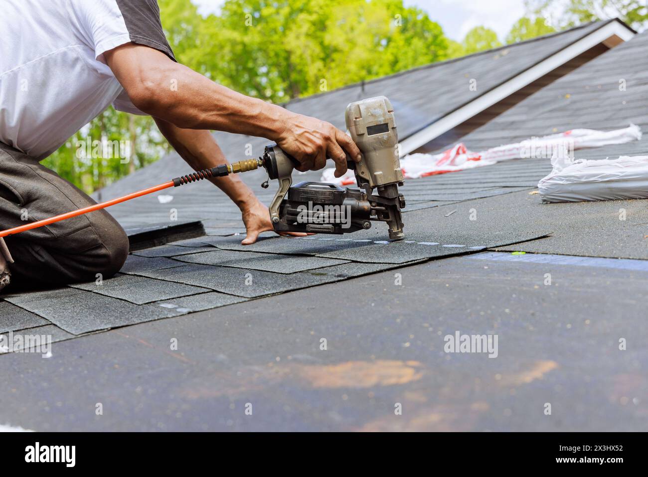 In addition to using an air pneumatic nail gun, roofer installs new ...