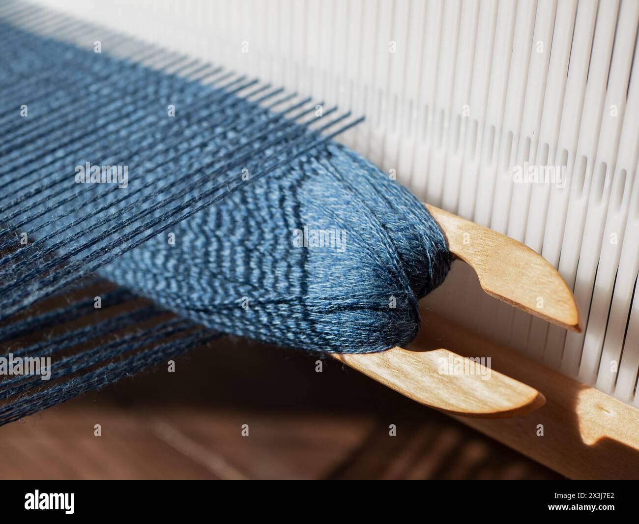 Wooden weaving shuttle with blue yarn is inserted in open shed ...