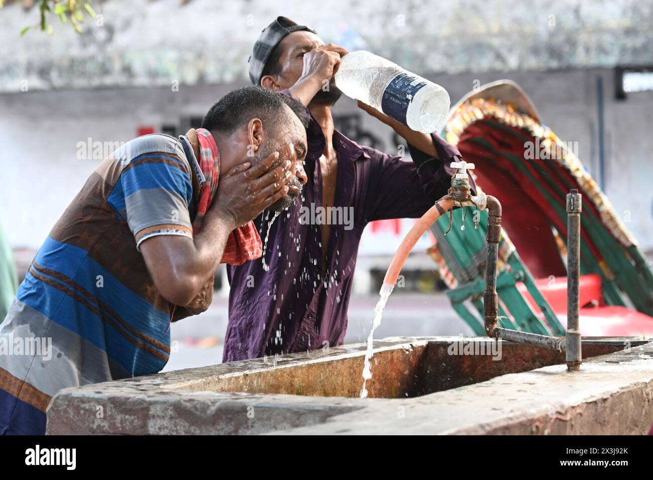 A rickshaw driver washing his face with water at a roadside water ...