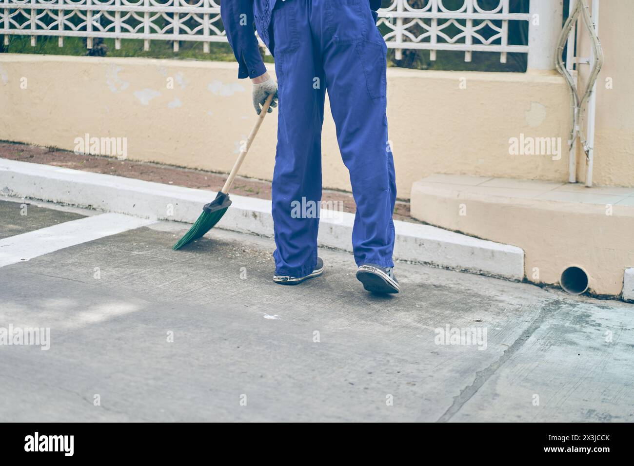 A male janitor sweeps a parking space next to a shopping center with a ...