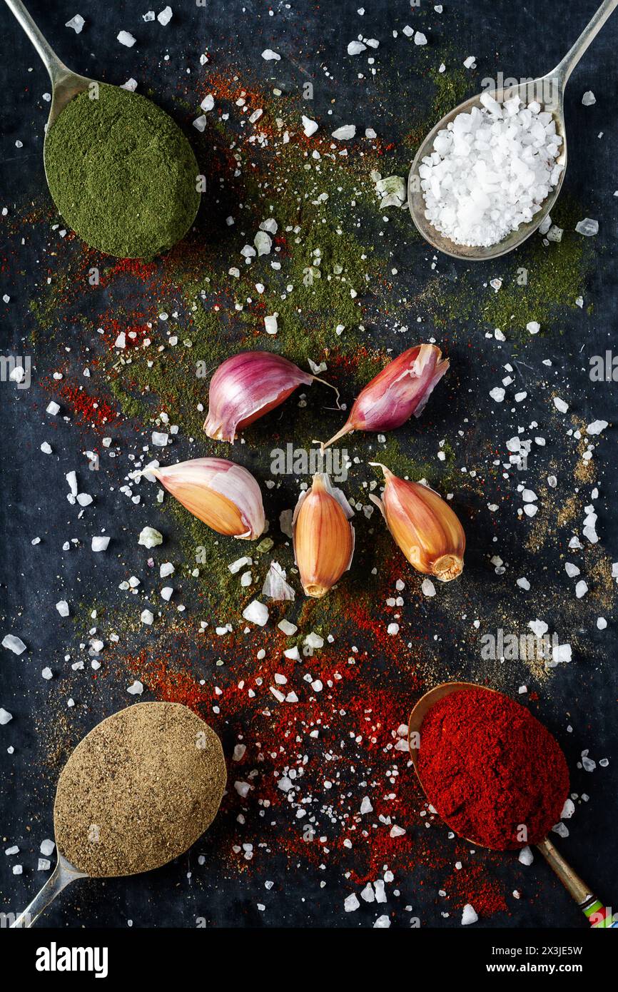 Spoons with spices and salt on black background sprinkled with ...