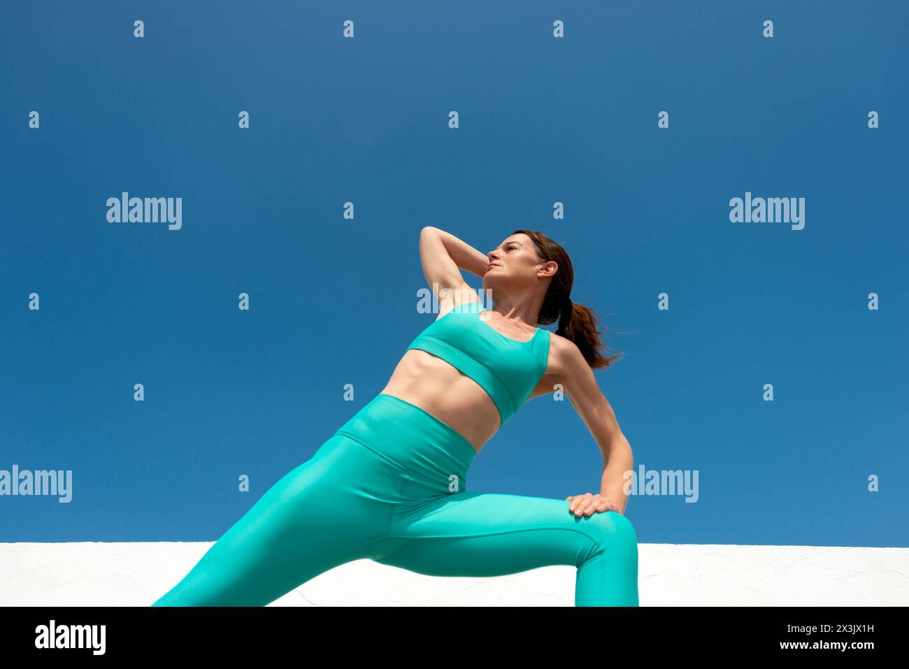 Mid adult woman doing a side angle body stretch, outside with blue sky ...