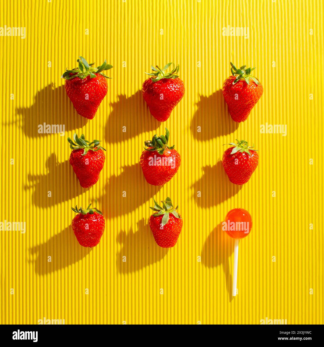 Strawberries pattern against yellow background with one lollipop ...
