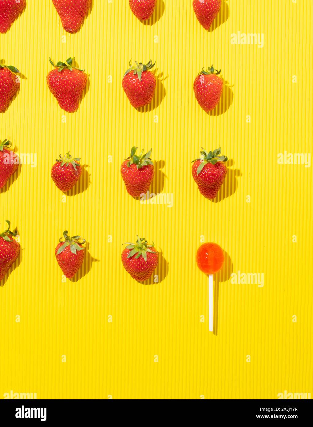 Strawberries pattern against yellow background with one lollipop ...