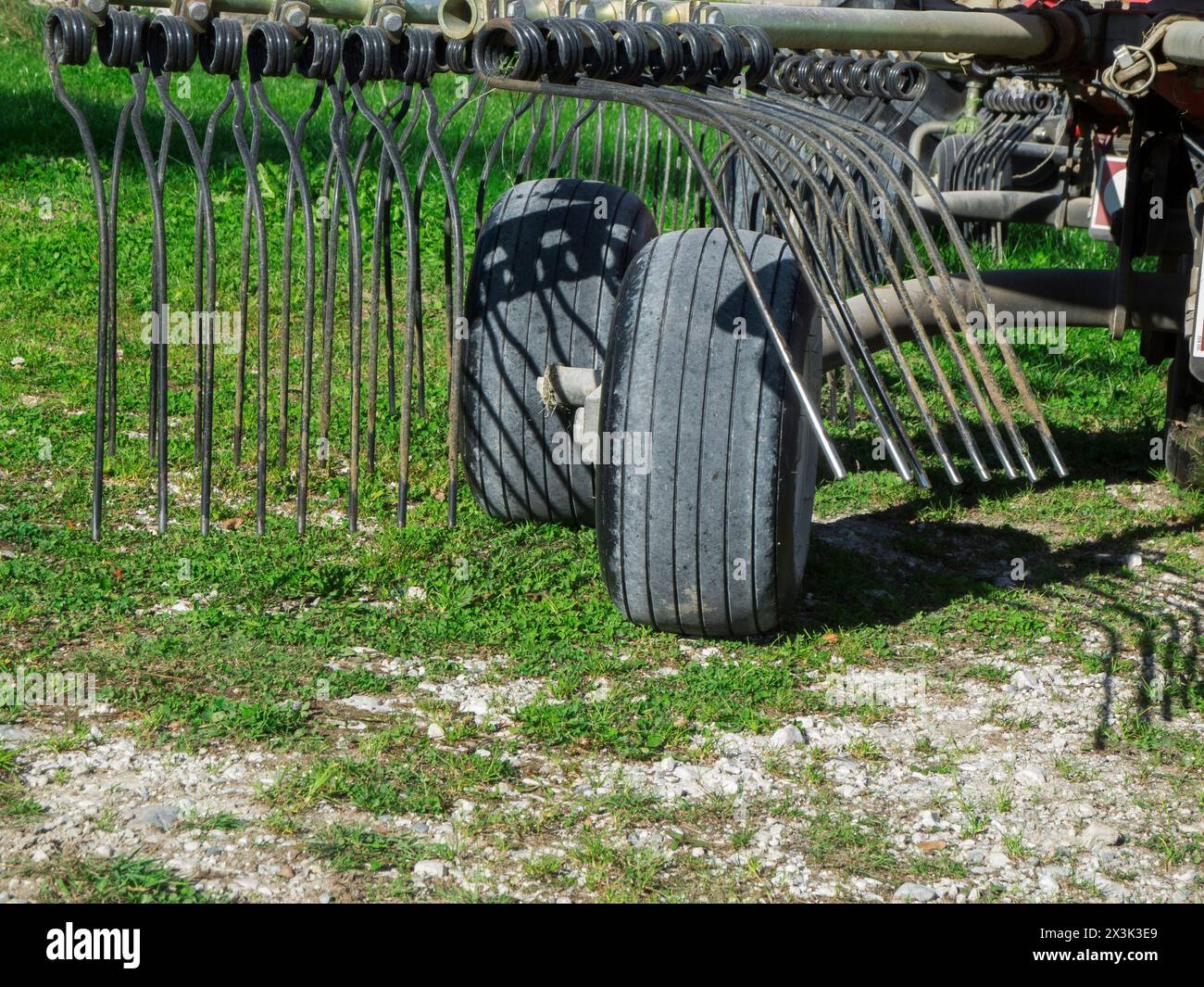 Partial view of two wheels and tines of a hay tedder on a gas surface ...