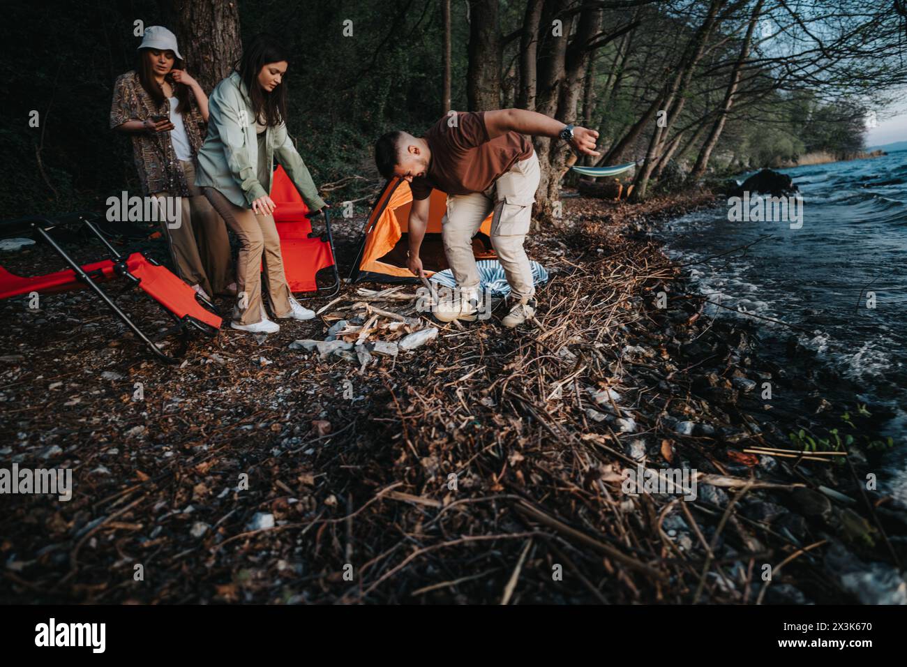 Group of friends setting up campfire by the lakeside during a camping ...