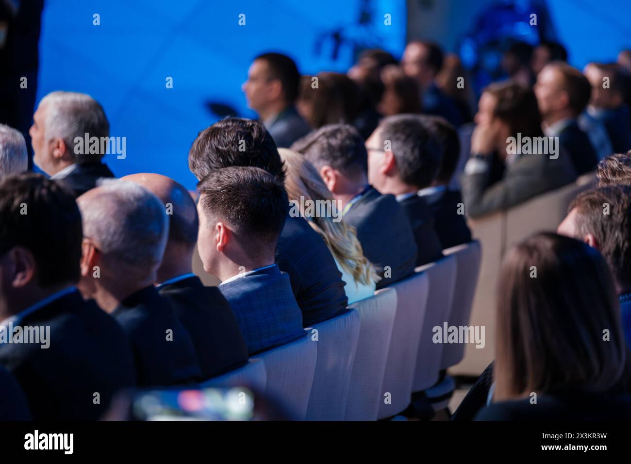 Professionally dressed audience members at a corporate event are ...