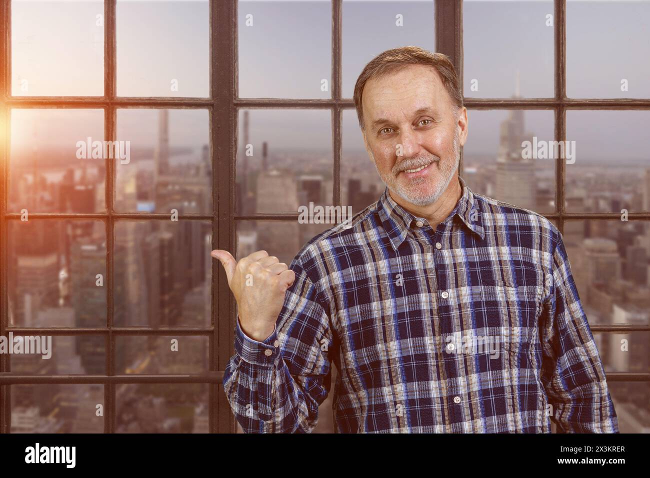 Portrait of smiling mature man pointing back with his thumb up ...