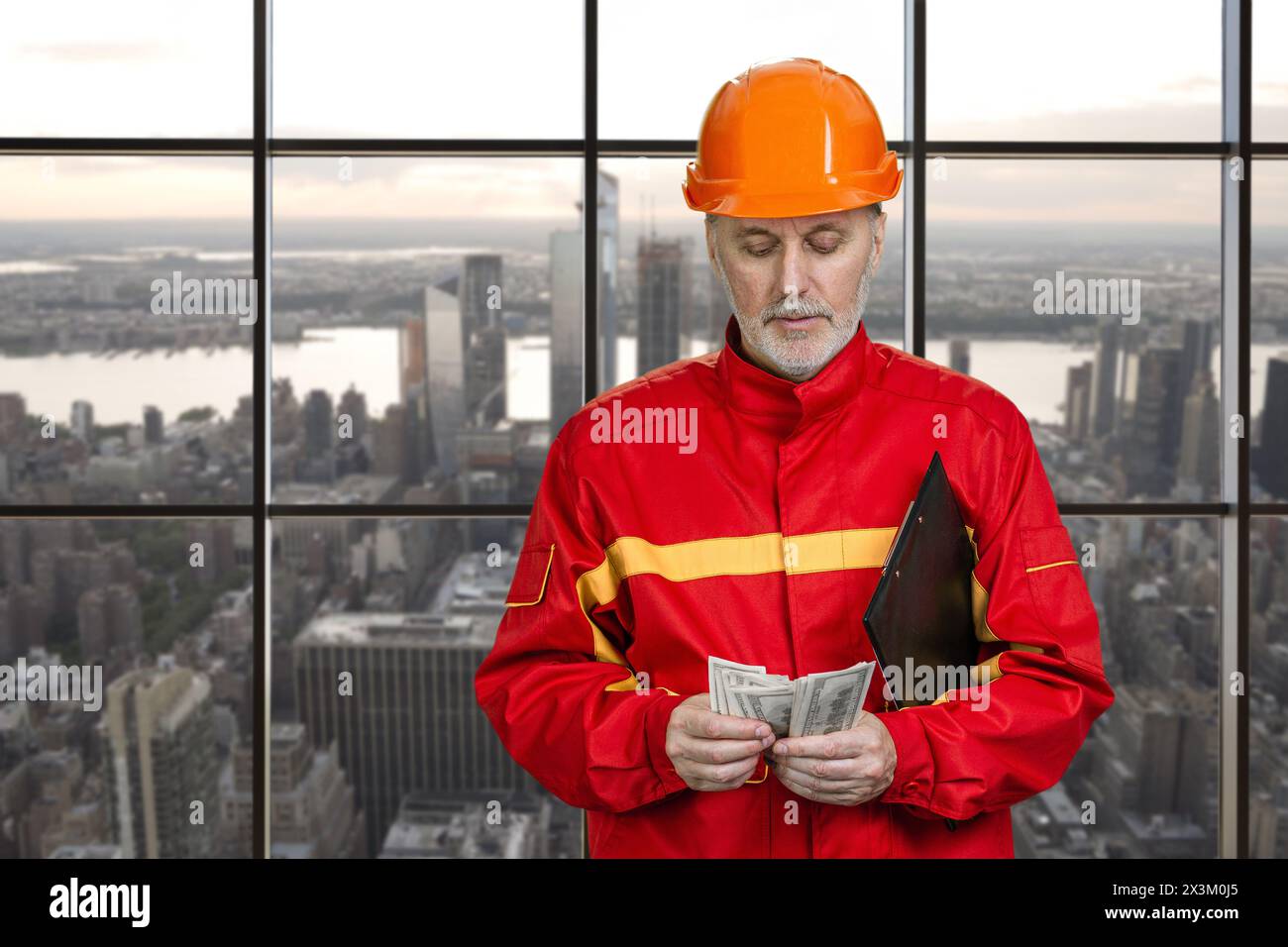 Portrait of construction worker in red uniform is counting money. Urban ...