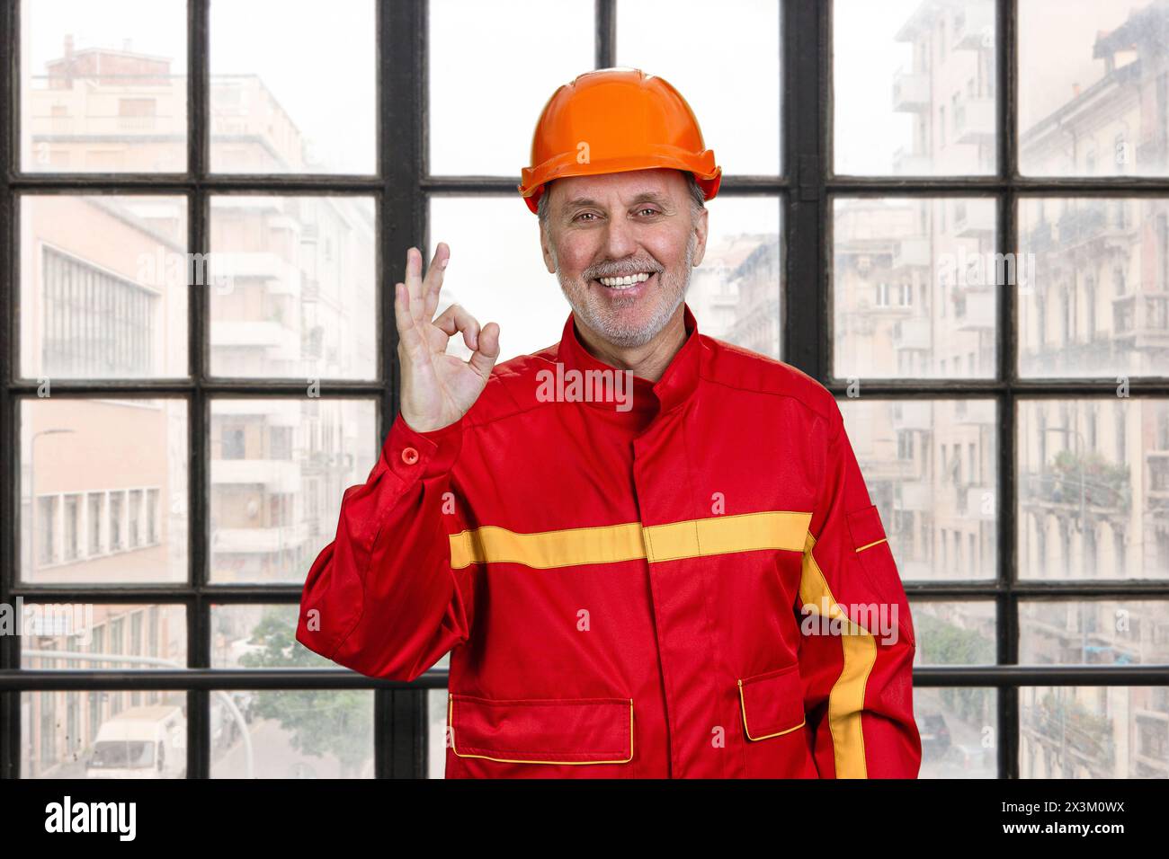 Smiling construction handyman worker in red uniform shows okay gesture ...