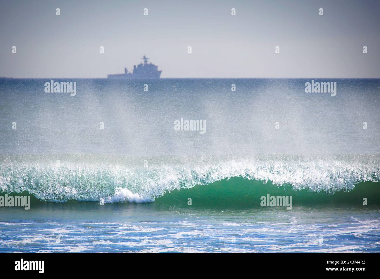 The Pacific Ocean surf rolls in, while a Navy ship sits on the distant ...