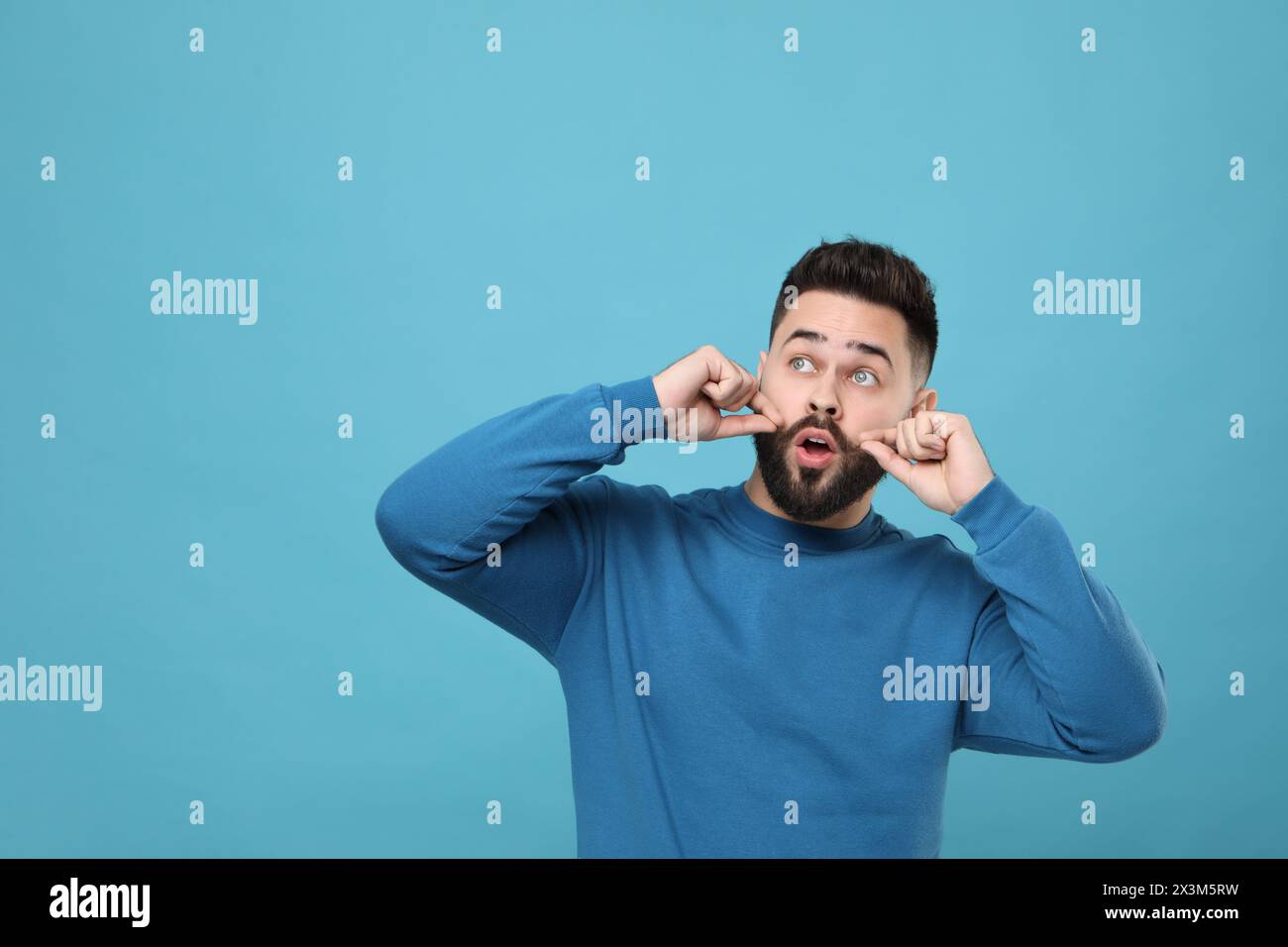 Surprised young man touching mustache on light blue background Stock ...