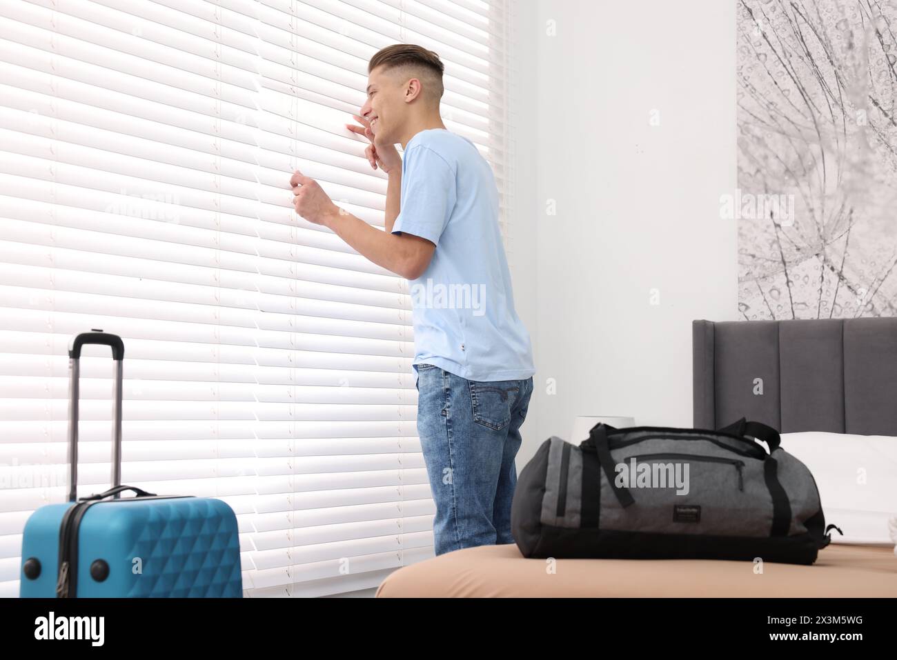 Smiling guest looking through blinds in stylish hotel room Stock Photo ...