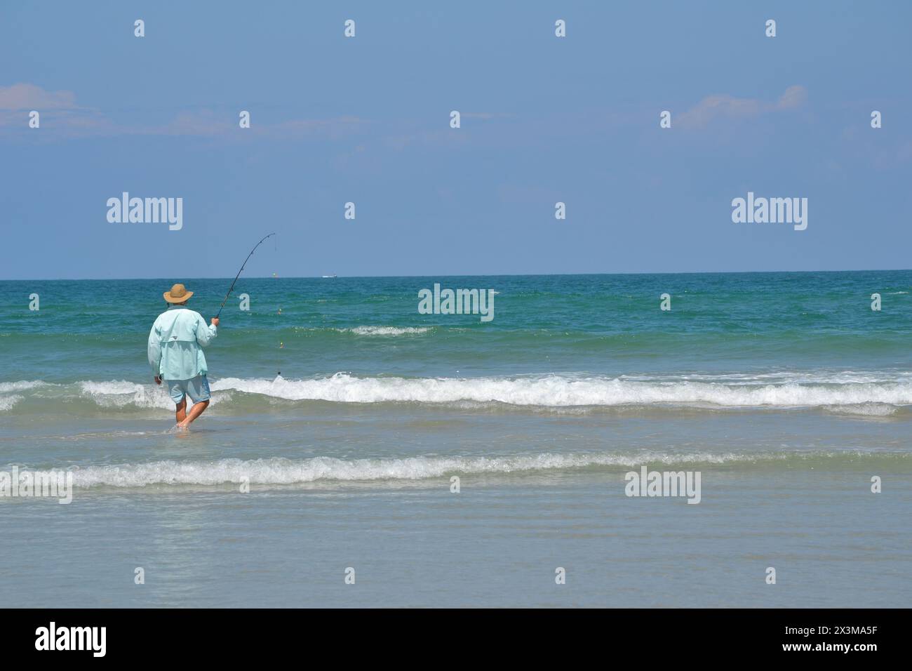 A surf fisherman walks knee-deep in the ocean at the edge of Ponce ...