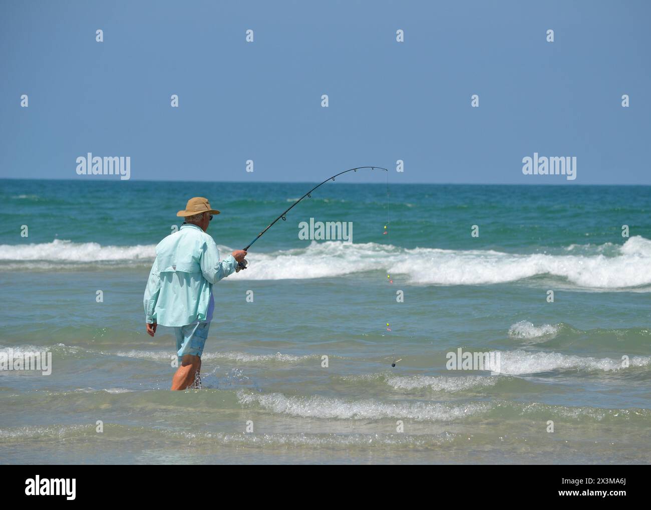 On the brink of the ocean, a surf fisherman strides into the waters of ...