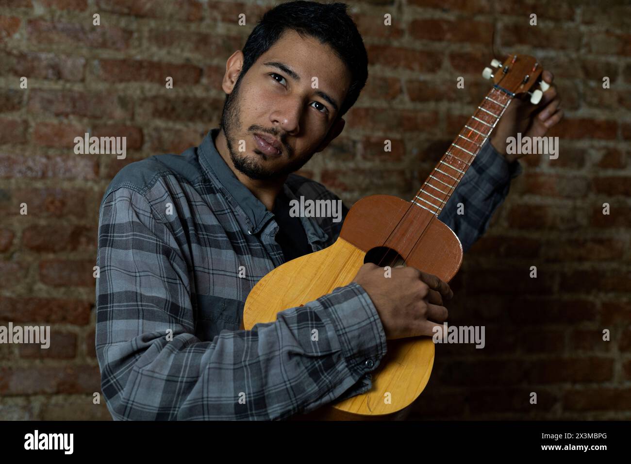 Latin American young man (24) tunes the strings of a "Cuatro", a ...