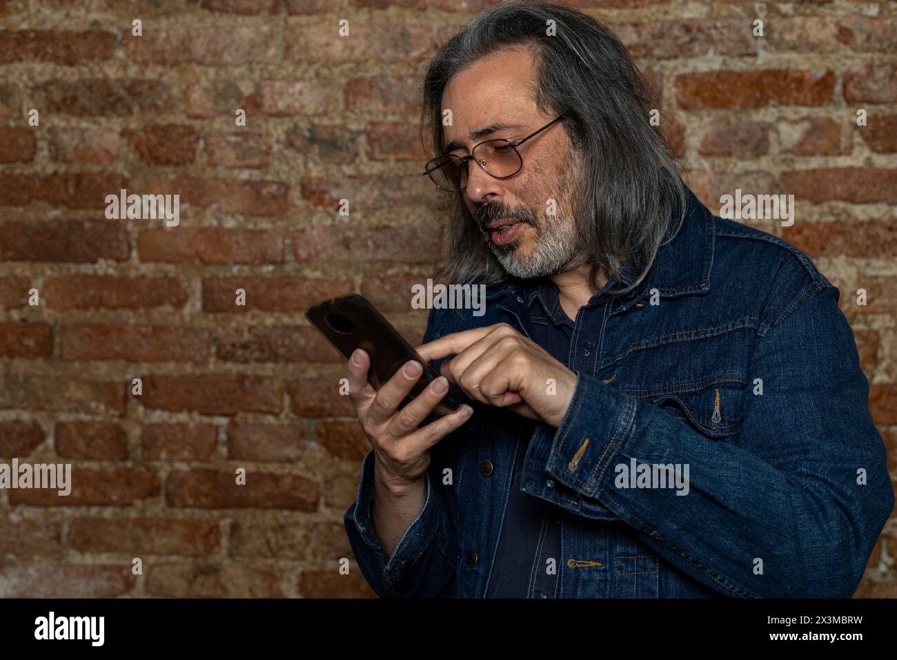 Latin American man (44) with long gray hair checks messages on his cell ...