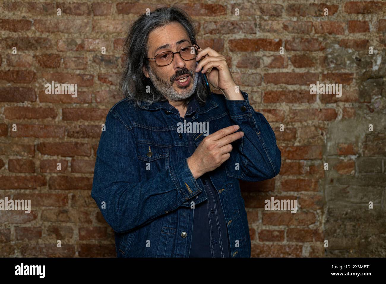 Latin American man (44) with long gray hair talking on his cell phone ...
