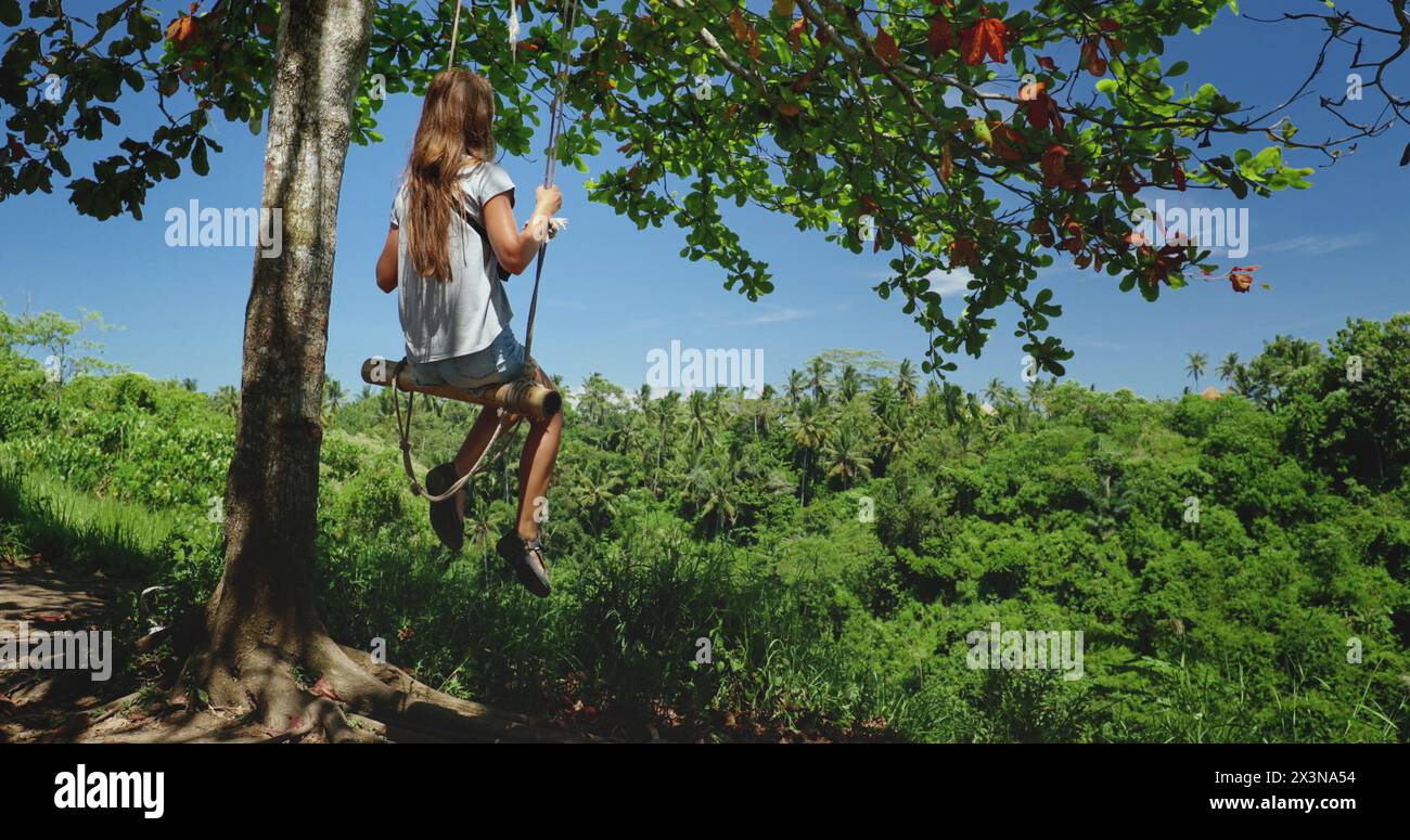 A woman is seated on a swing hanging from a tree in Bali, specifically ...