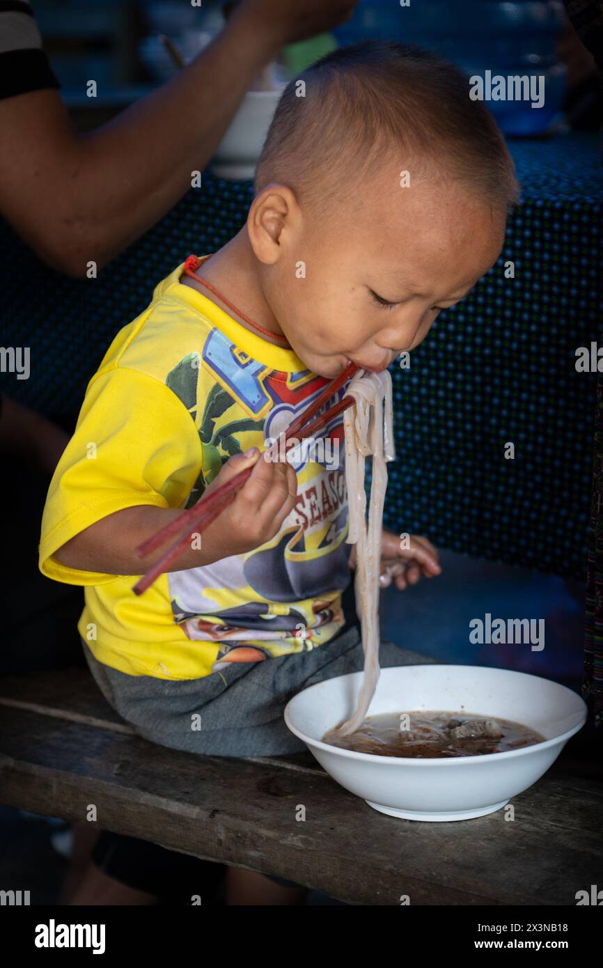 Young boy eating noodles at the Can Cau Market in Lao Cai Province ...