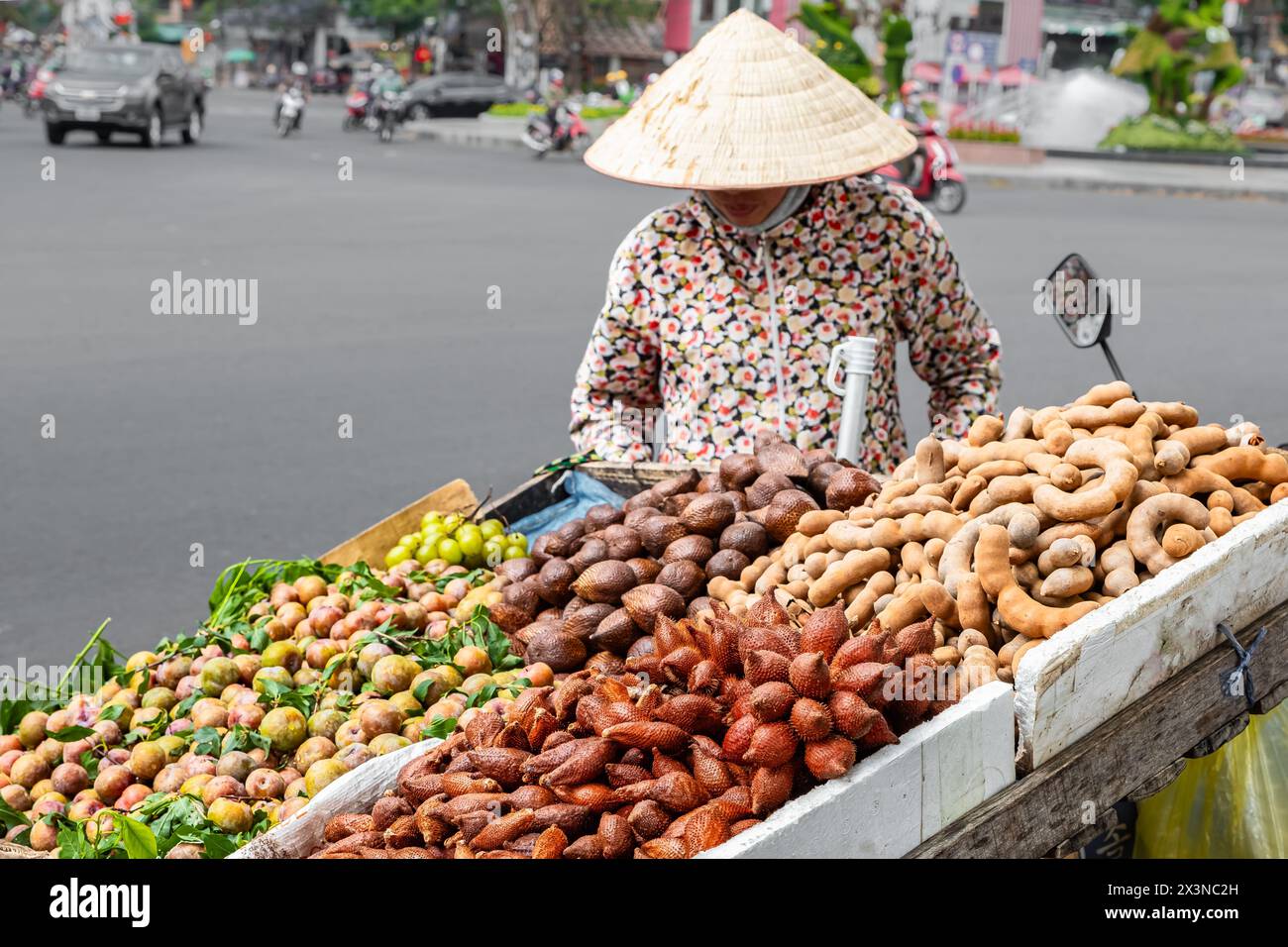 A woman wearing traditional Vietnamese clothing sells fruit and ...