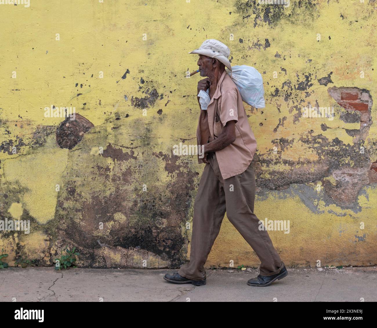 A man smoking a cigar walking in front of a yellow painted, weathered ...