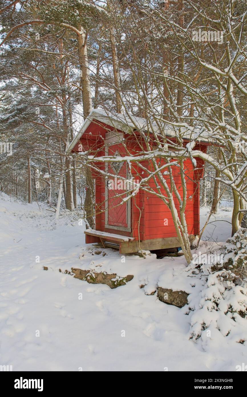 Small wooden red painted outdoors toilet in forest in winter with snow ...
