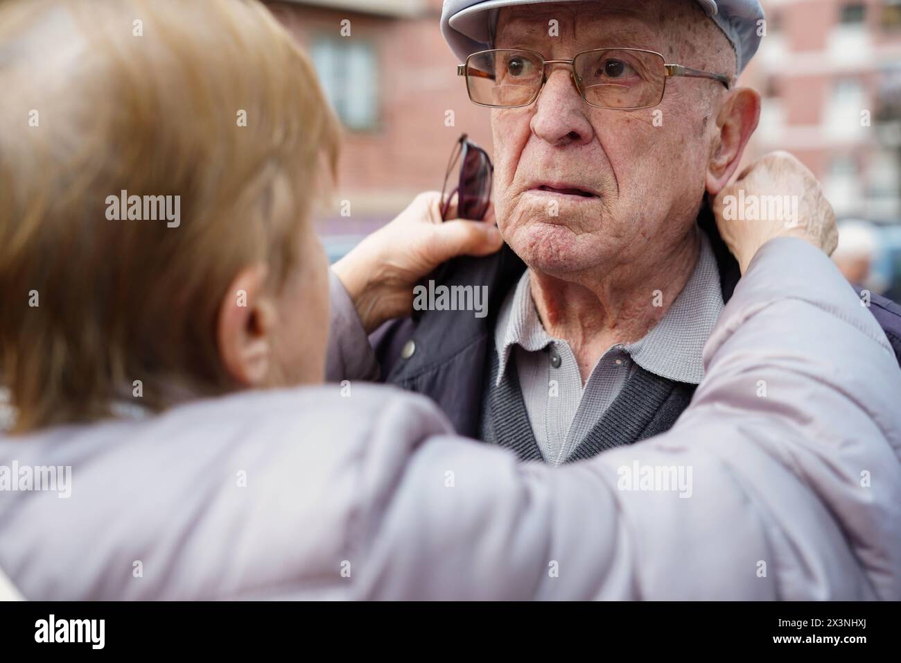 an old woman helps his husband get dressed outside. dependency and care ...