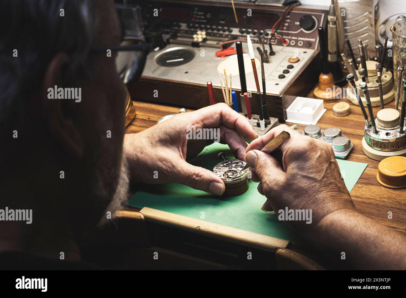 Shot from behind a watchmaker at his workbench full of tools and his ...