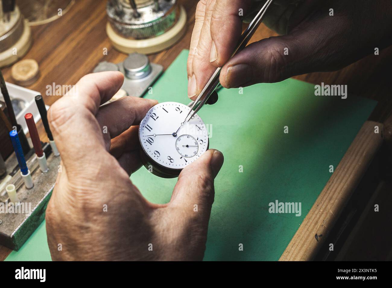 Close-up of a watchmaker's hands using tweezers to put the hour hand of ...