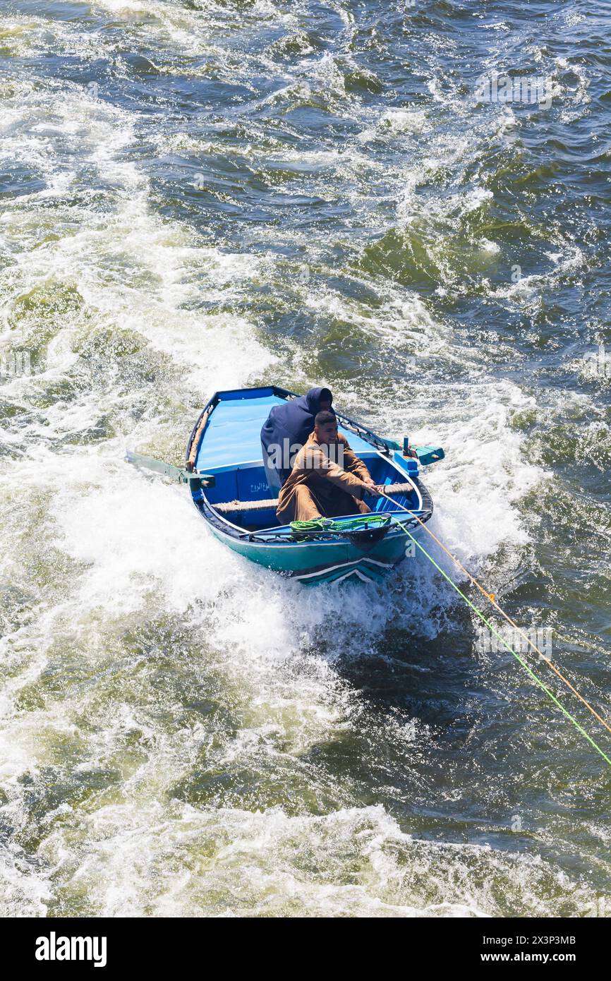 Two Egyptian men in a rowing boat, taking a tow from a passing Nile ...