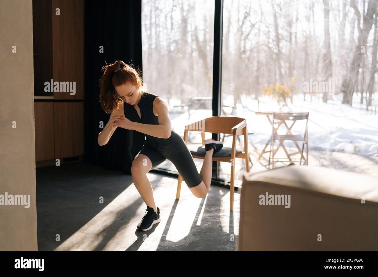 Sportive slim female doing single leg lunge using chair in living room ...