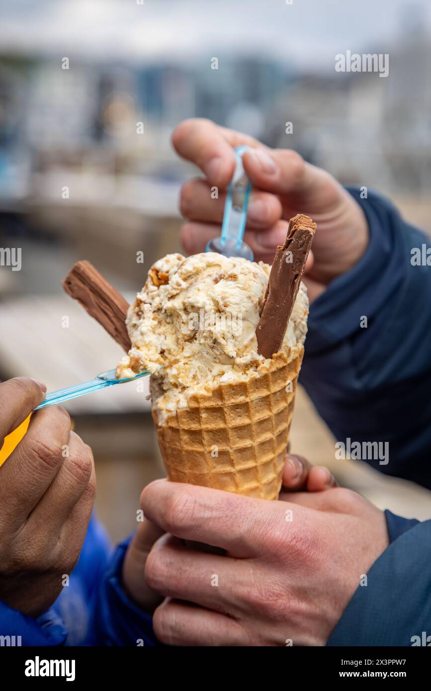 A close up of two people sharing an ice cream cone, with a shallow ...