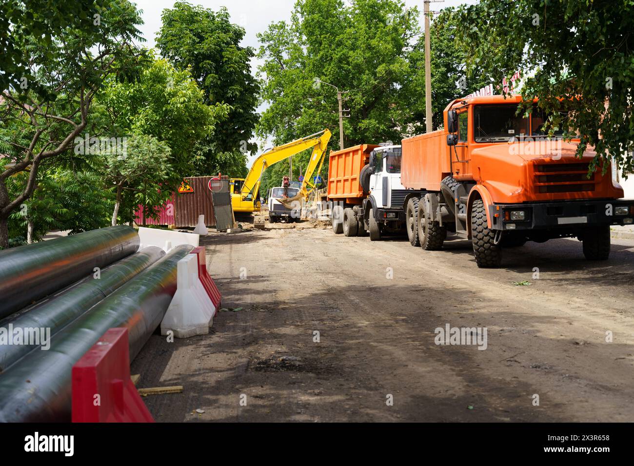 Trucks and an excavator work at a road construction site, with pipes ...