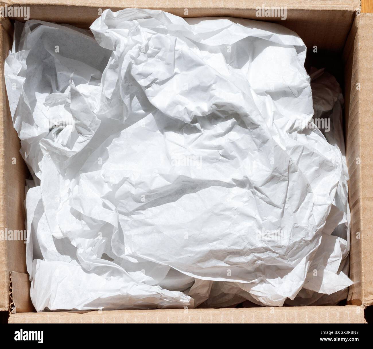 Cardboard box filled with shipping packaging paper on a wood floor ...