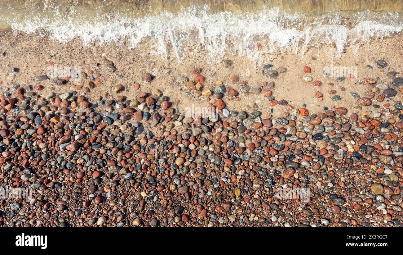 Flat lay view of shore with foamy sea wave and polished brownish red ...