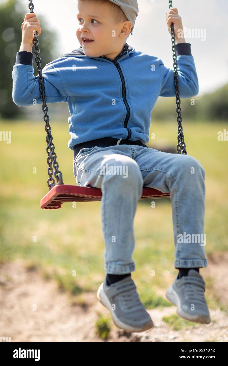 A cute little boy in a blue sweater swinging on a chain swing. The ...