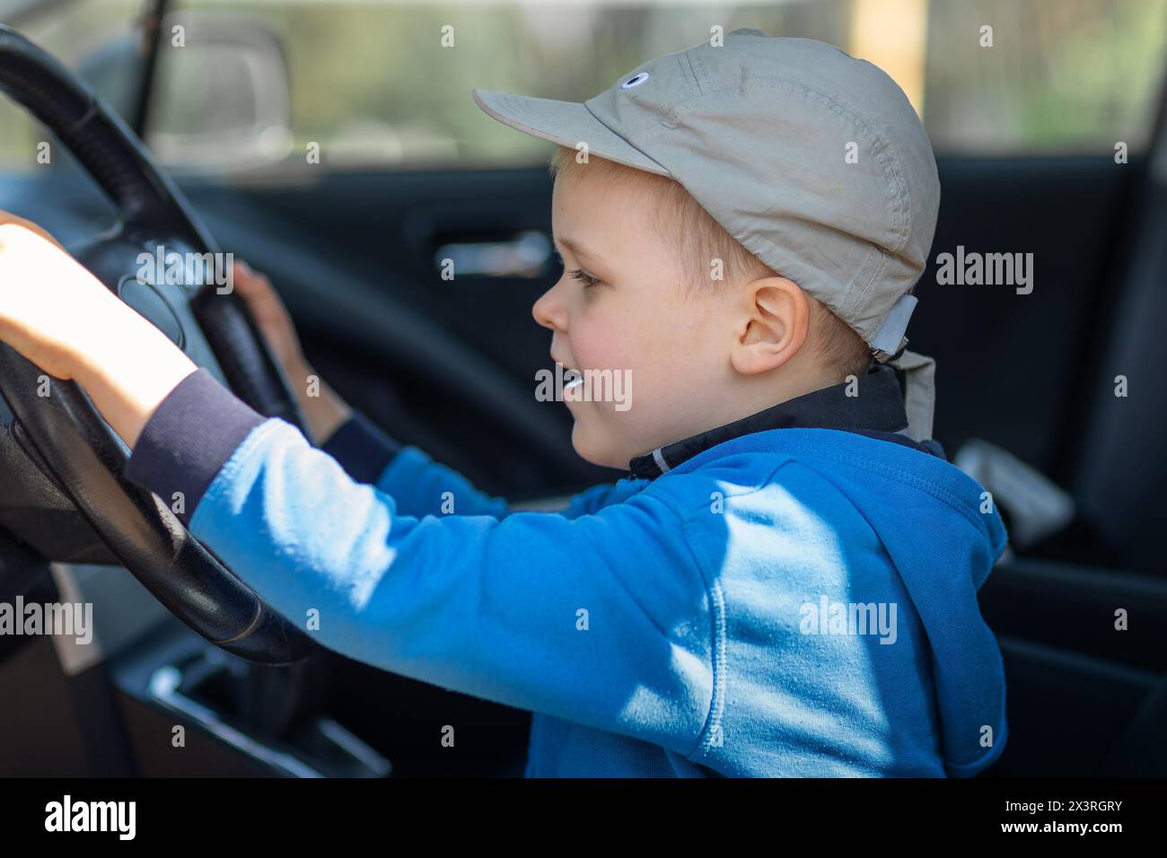 Cute little boy behind the wheel of an fathers car, he holds the ...