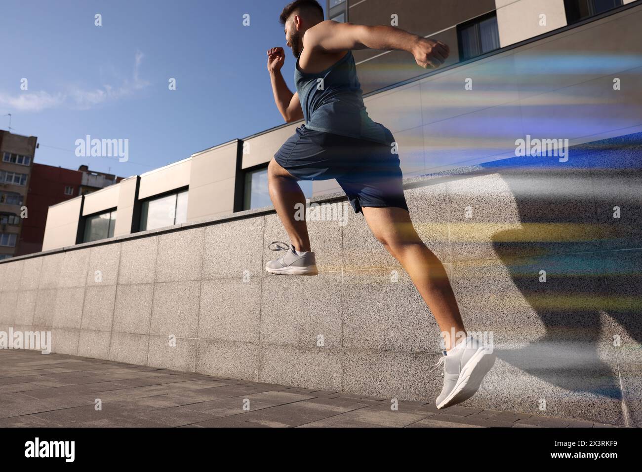 Sporty young man running on street, low angle view. Light trails ...