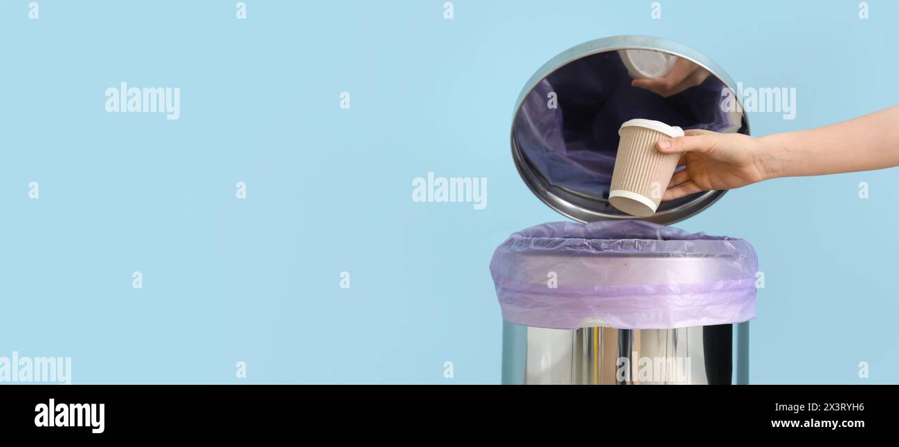 Female hand throwing paper cup into trash bin on light blue background ...