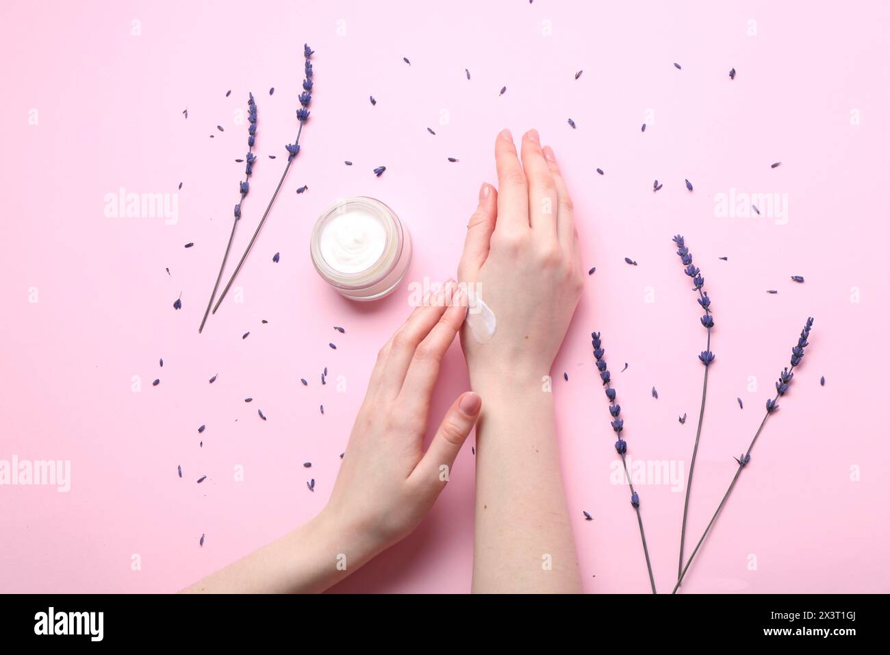 Woman applying hand cream and lavender flowers on pink background, top ...