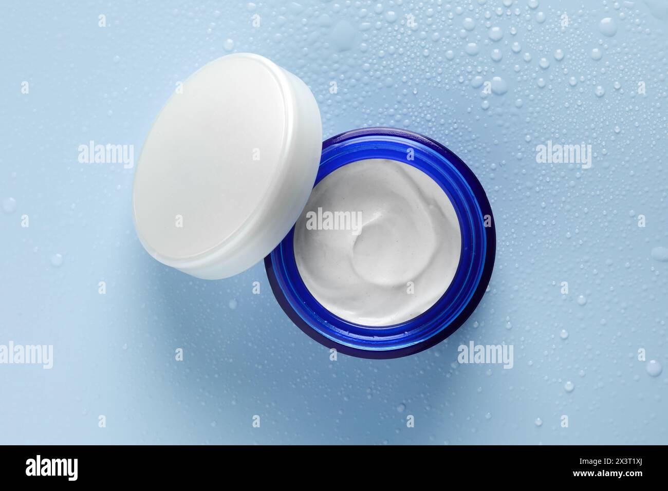 Moisturizing cream in open jar on light blue background with water ...