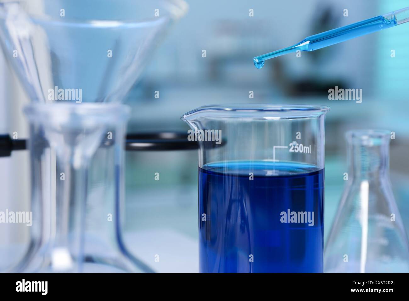 Laboratory analysis. Dripping blue liquid into beaker on table, closeup ...