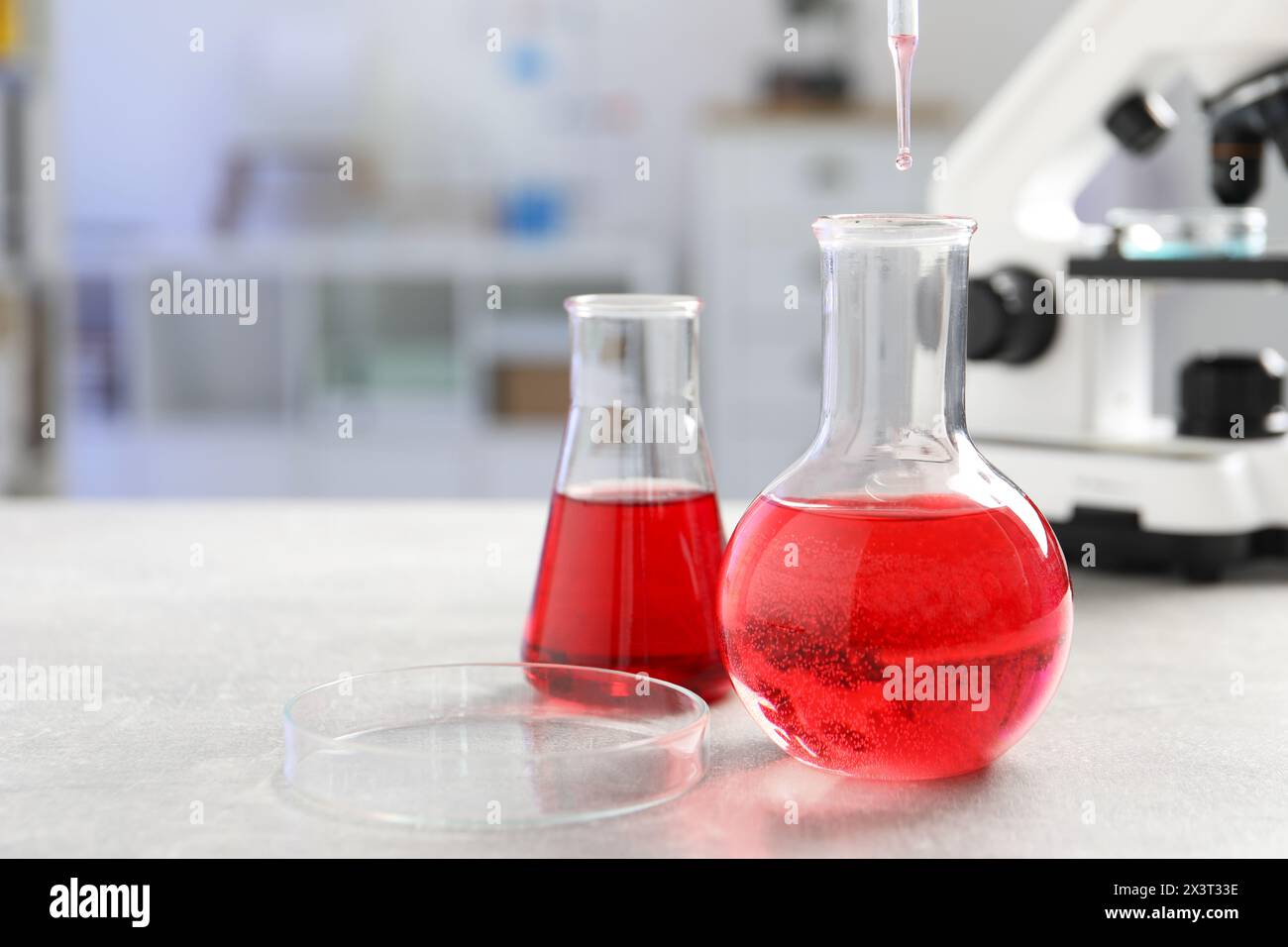 Laboratory analysis. Dripping red liquid into flask at light grey table ...