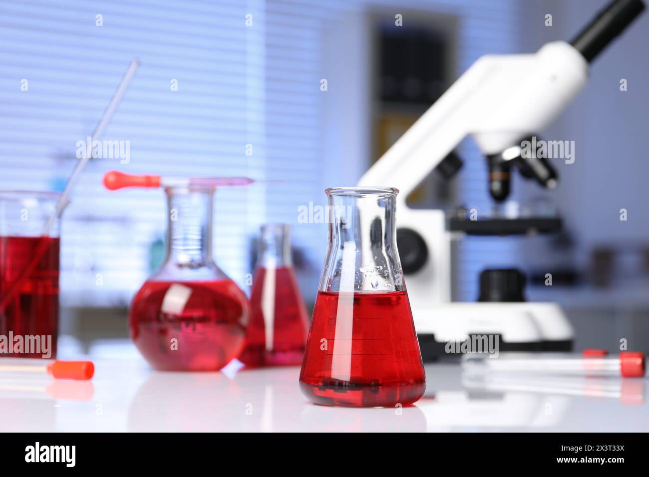 Laboratory analysis. Glass flasks with red liquid and microscope on ...